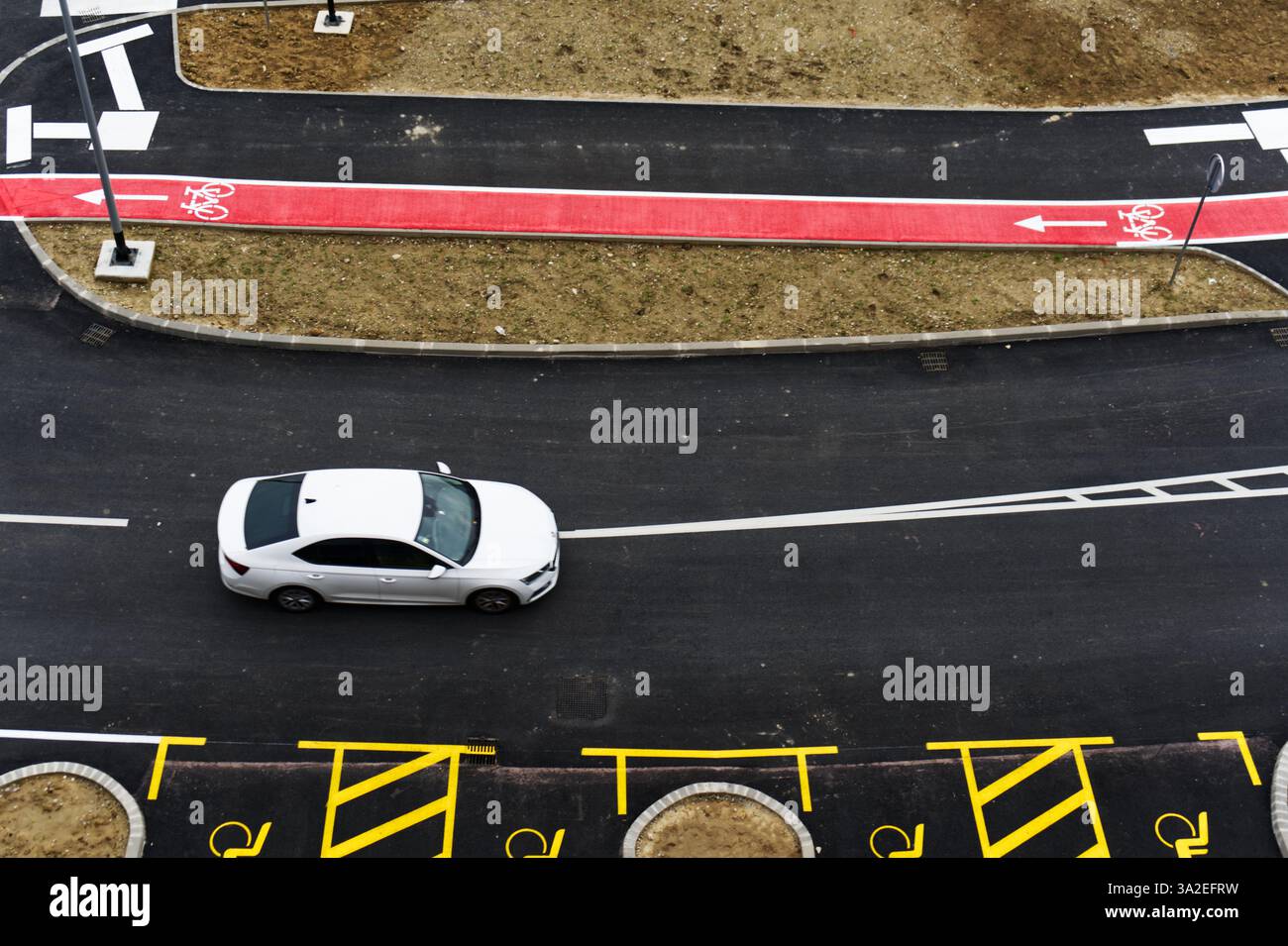 Aerial view of a white sedan driving on a newly paved road with marked ...