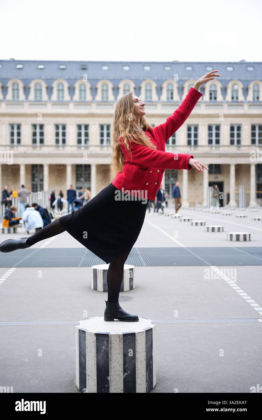 A stylish woman in a red coat and black dress strikes an elegant ballet ...