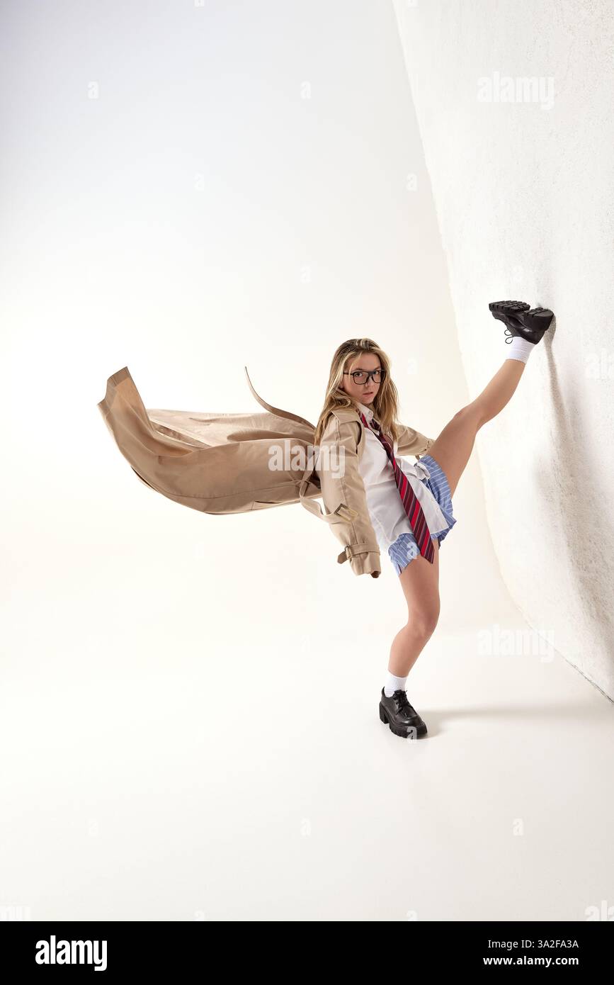 Stylish young blonde woman performing power pose, high kick, and wind ...