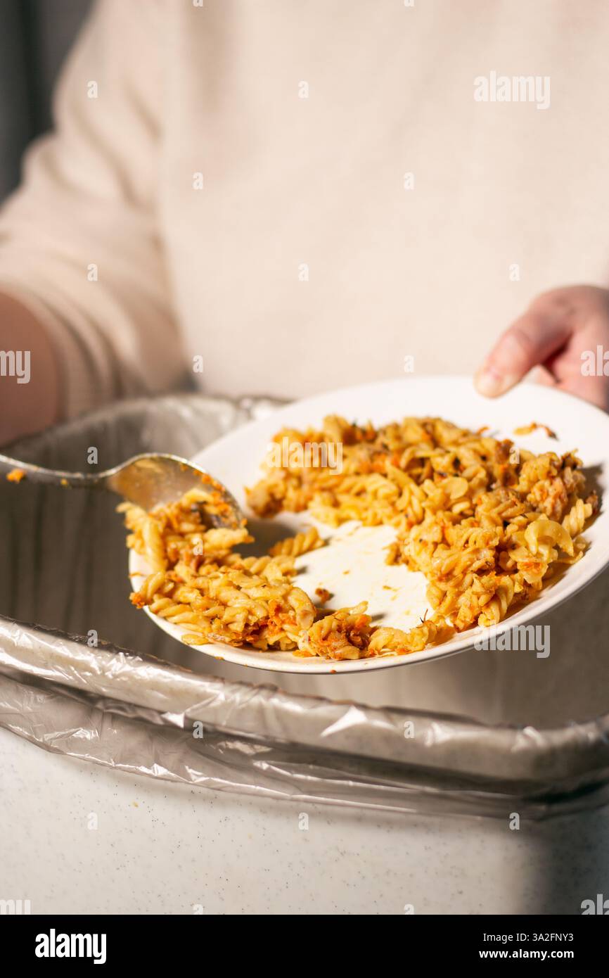 Vertical image of woman holding white plate with food leftovers and ...