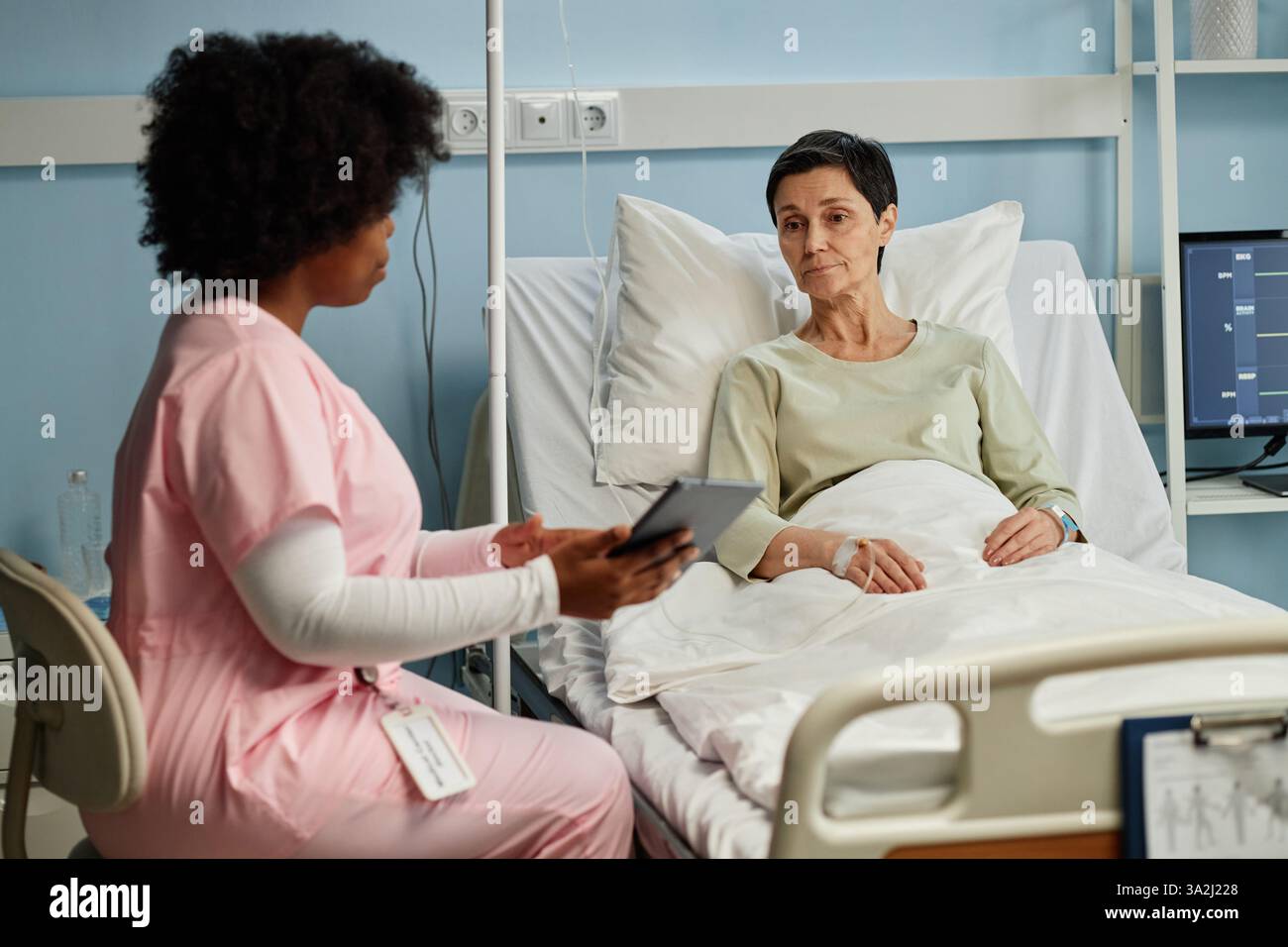 Nurse sitting beside a bed, holding a notepad, and interacting with an ...
