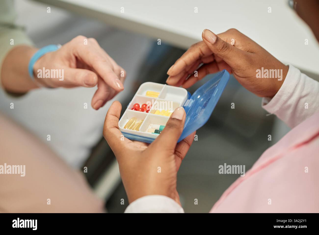 Close-up of two people sharing and organizing medications from a pill ...