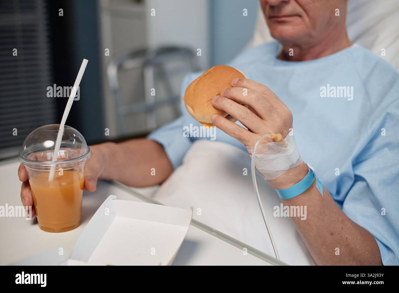 Senior person holding sandwich and juice while resting in hospital bed ...