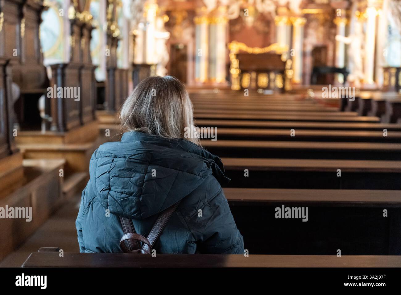 Woman sitting alone in historic church wooden pew, looking towards the ...
