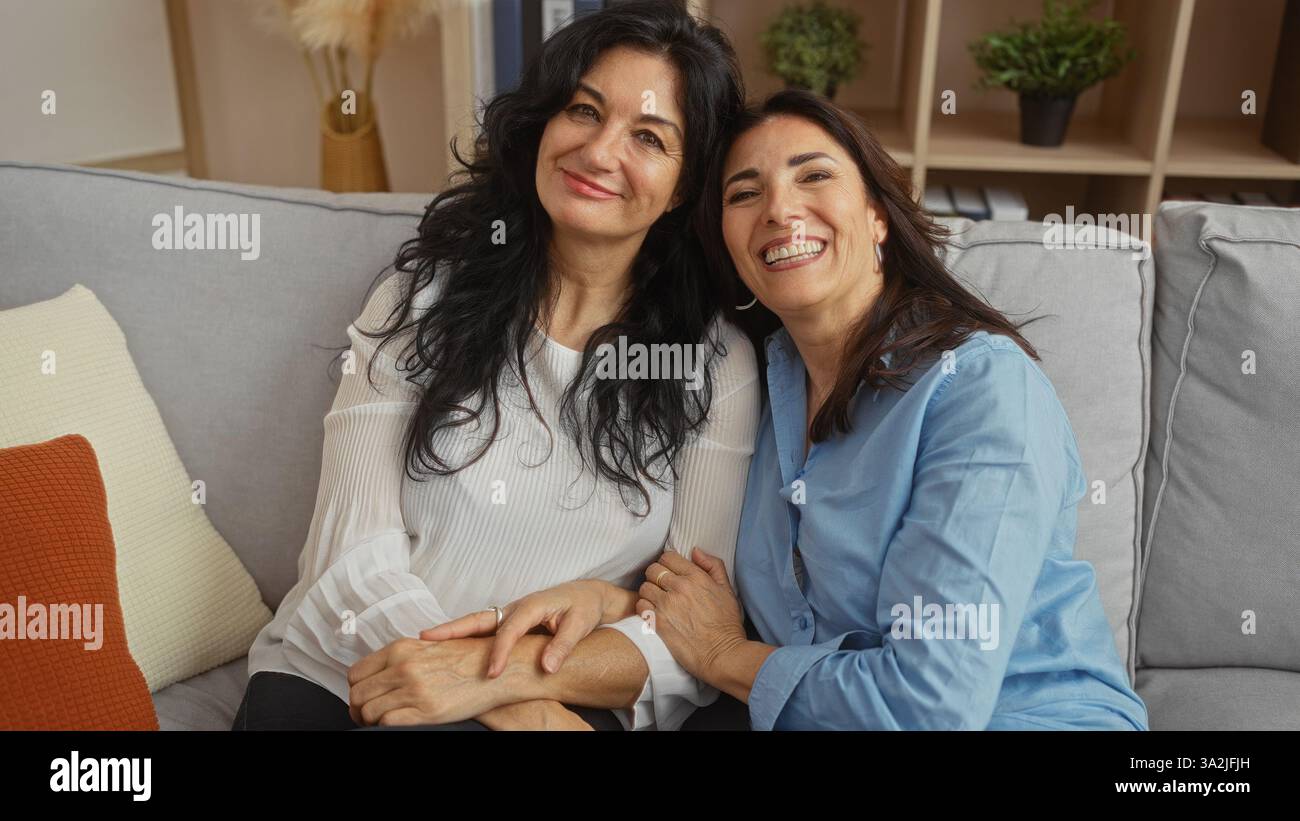Sisters sitting together on a sofa in a cozy living room, smiling ...