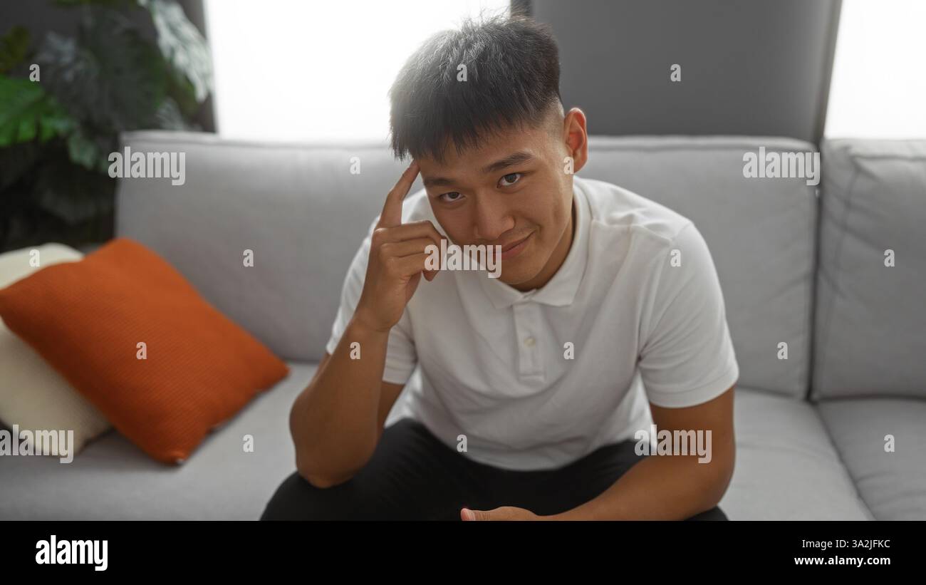 Young man seated in a living room smiles thoughtfully, with a modern ...