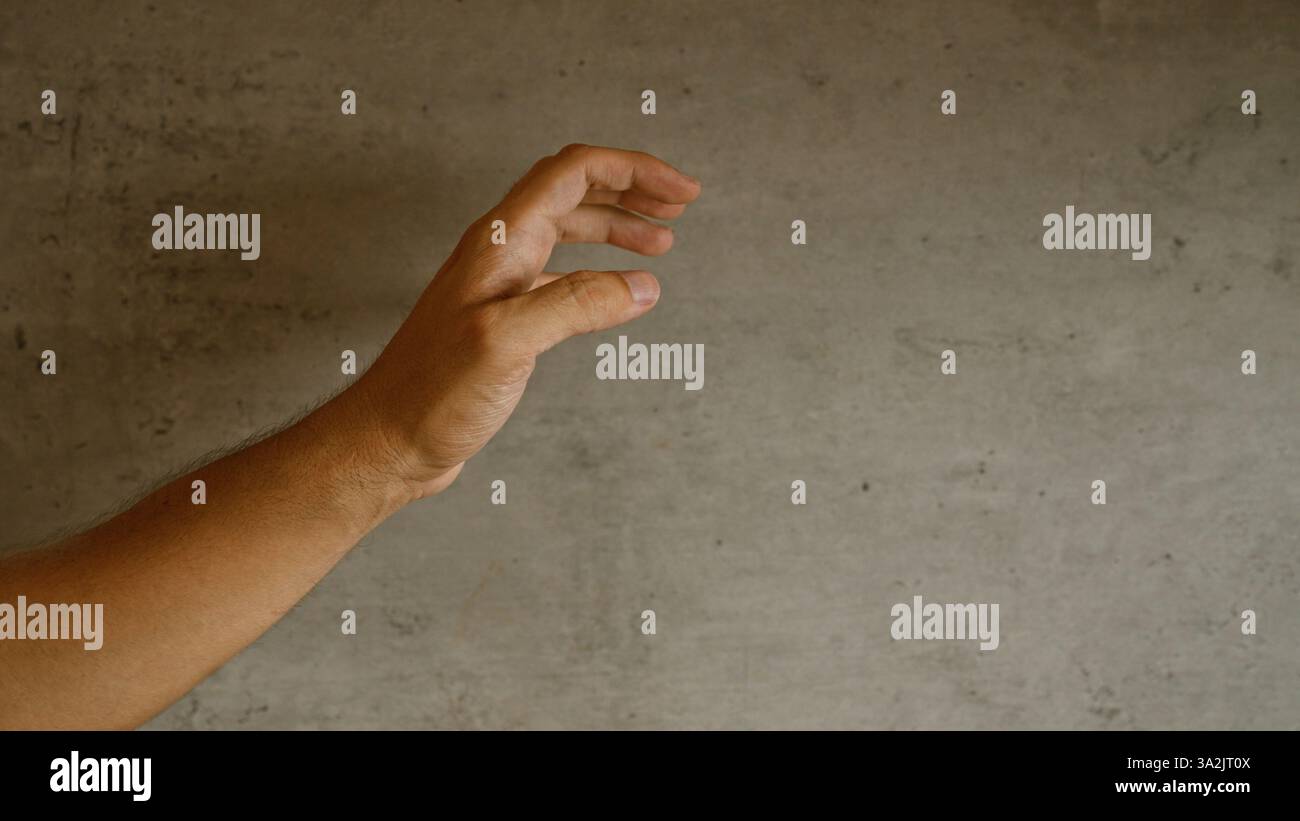 Man's hand with fingers extended against a concrete wall background ...