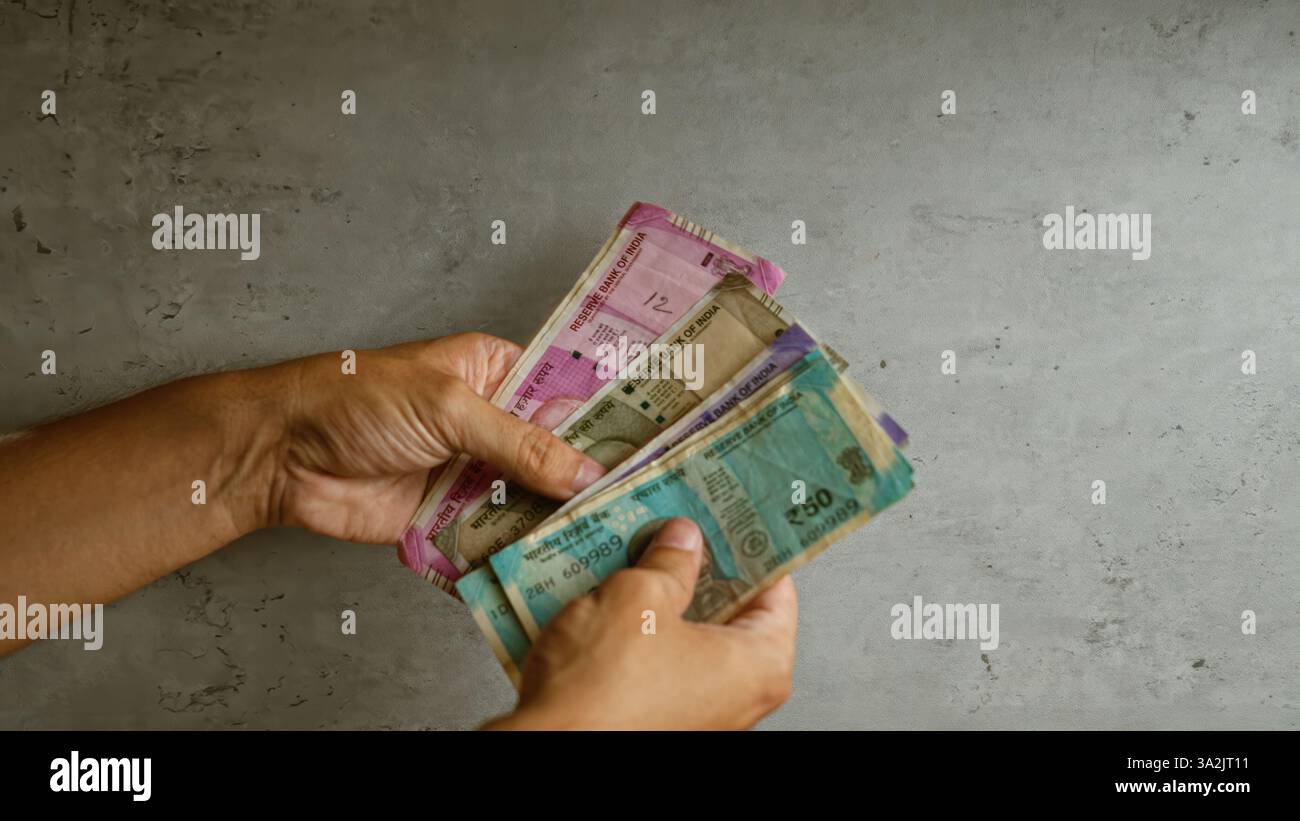 Hands counting indian rupee notes against a concrete background ...