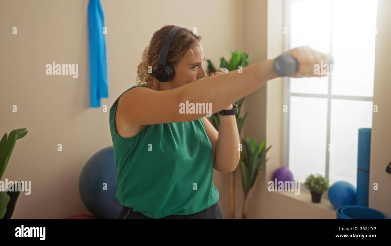 Young woman boxing with dumbbells in a gym wearing headphones ...