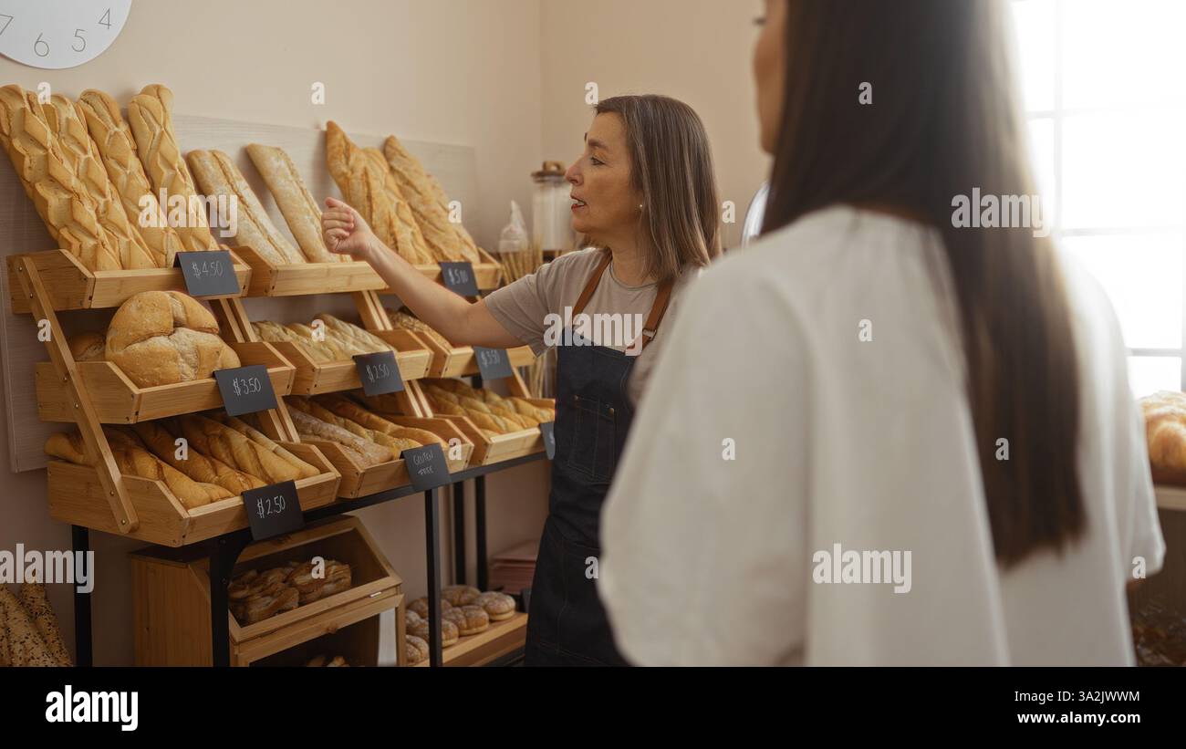 Baker explaining bread options to customer in bakery shop interior with ...