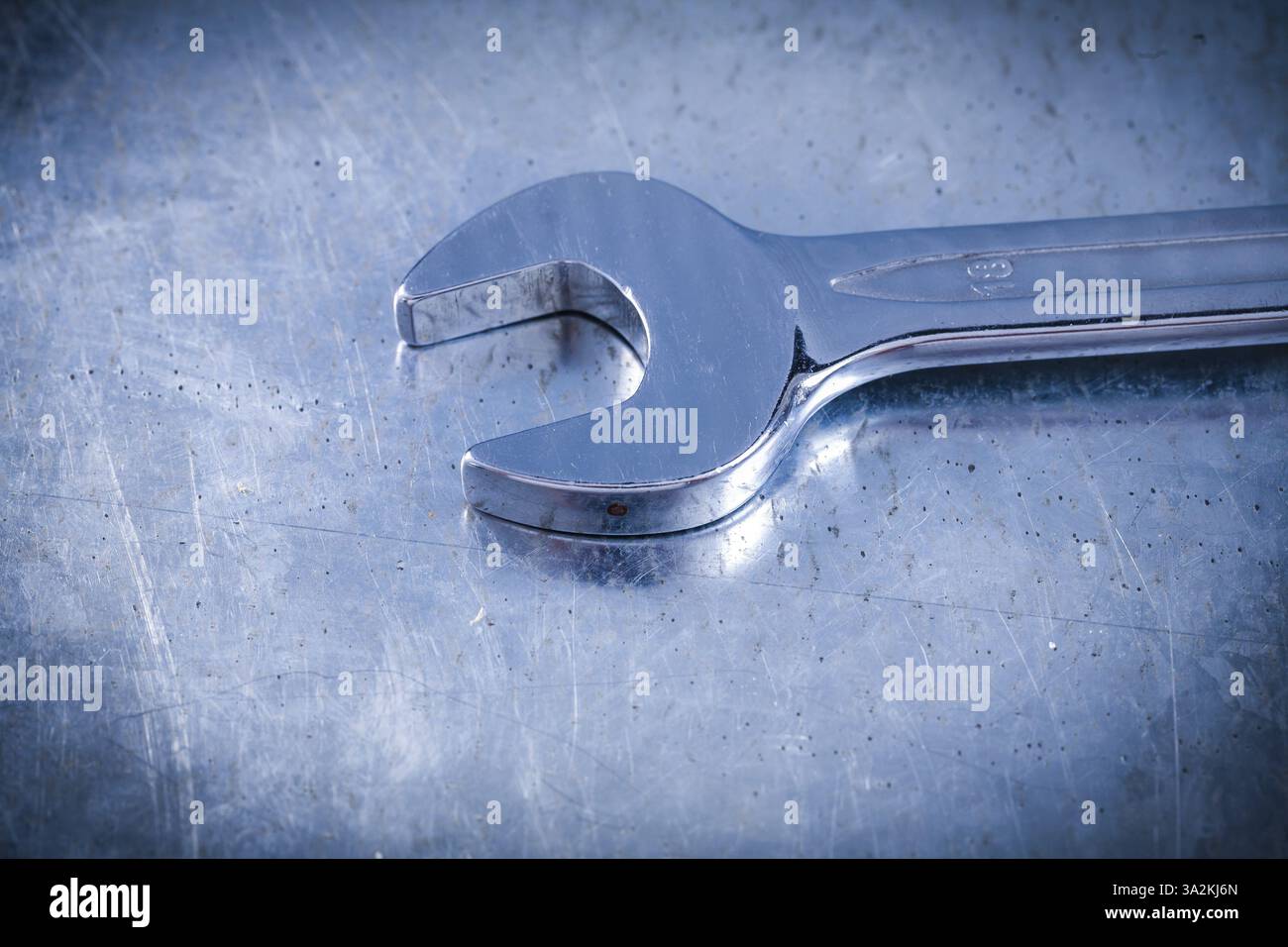 Stainless spanner wrench on scratched metallic background top view ...