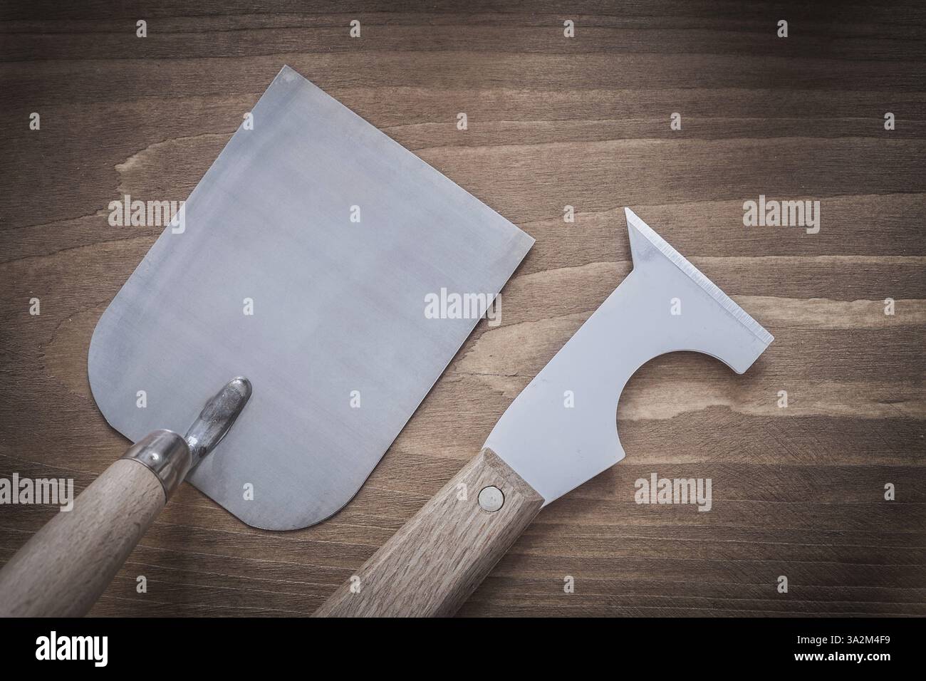 Sharp glossy paint scraper and bricklaying trowel on wooden surface ...