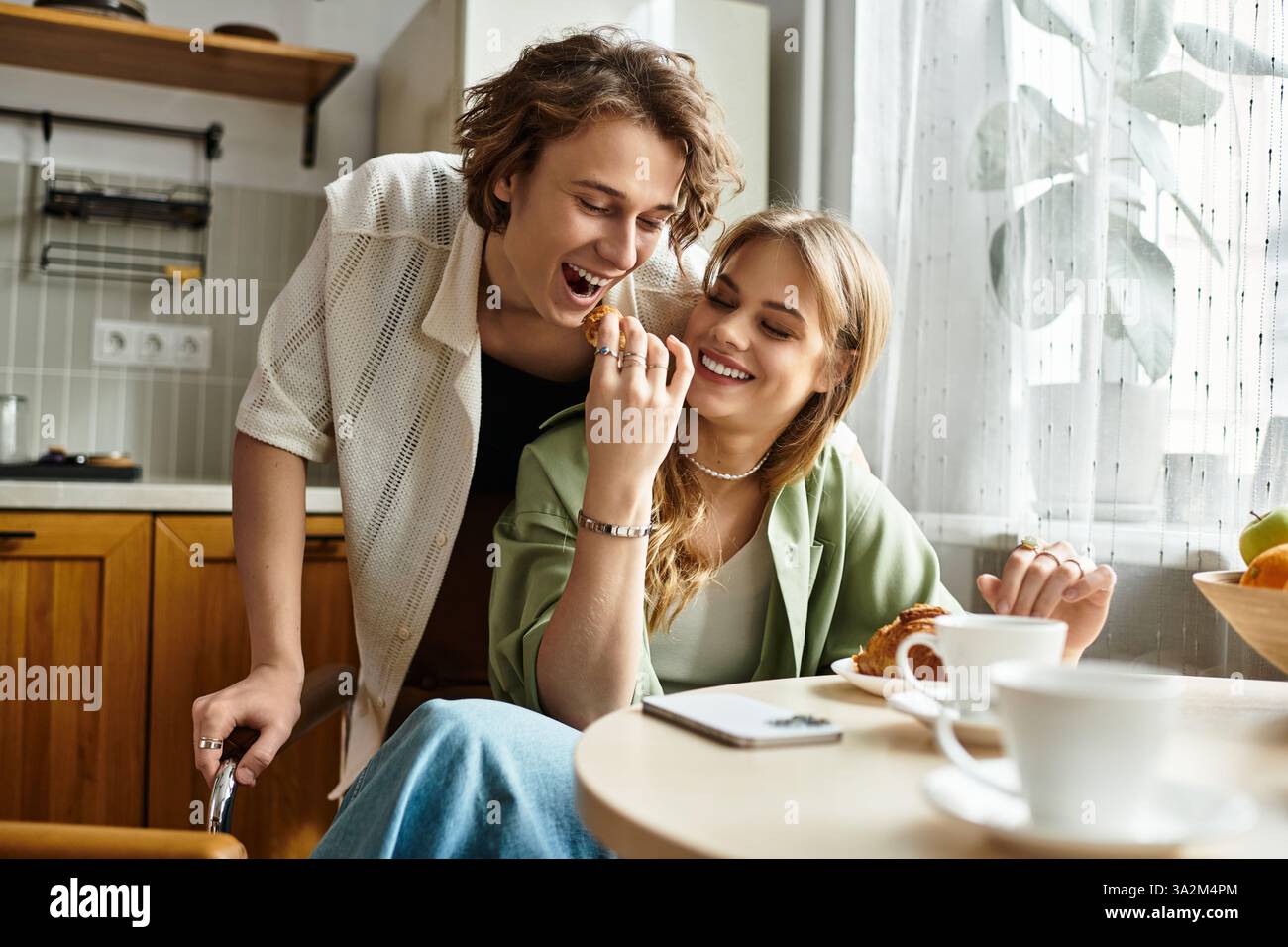 A loving couple smiles and playfully shares food in a modern, comfy ...