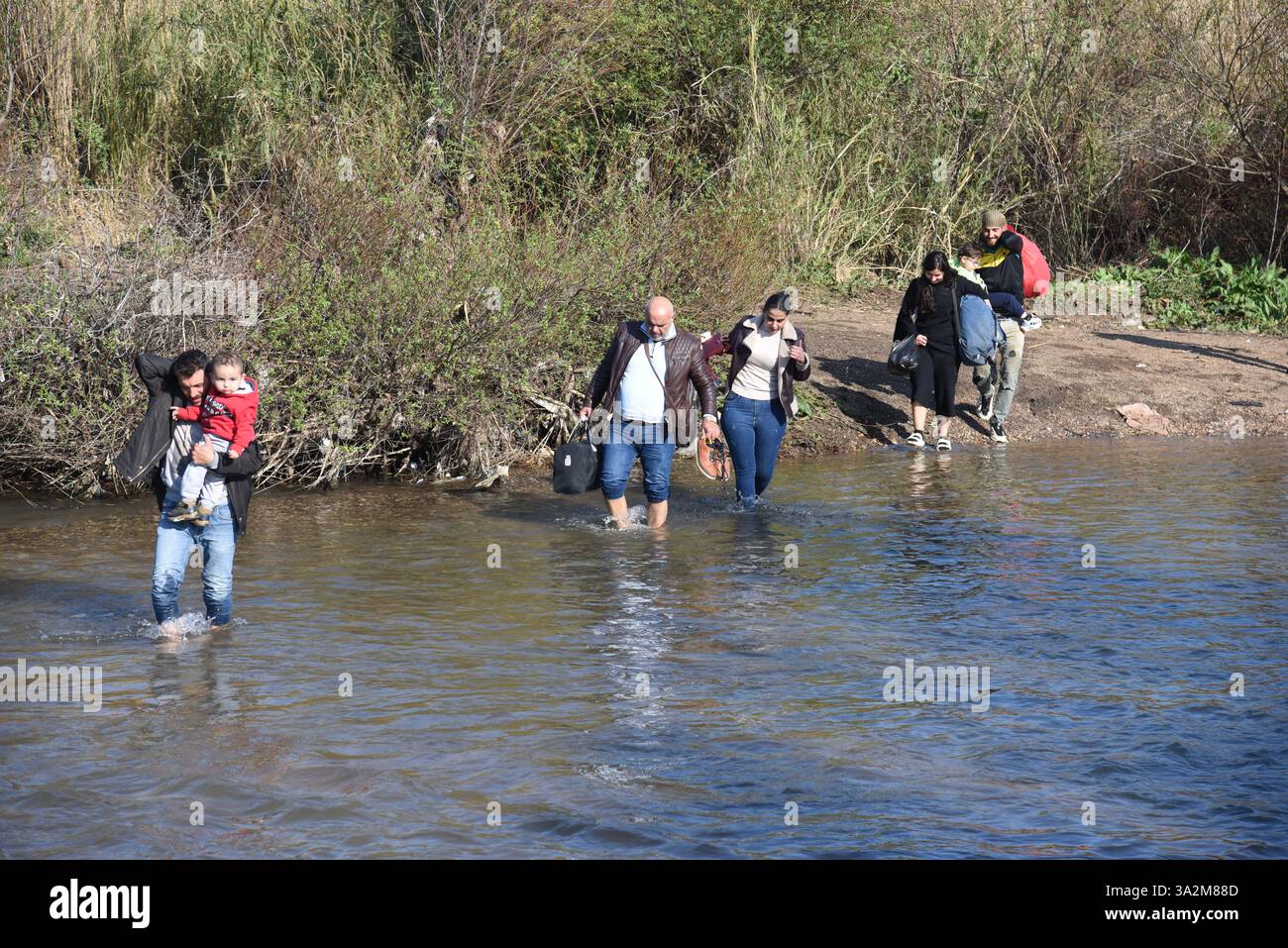 Akkar. 12th Mar, 2025. Syrian citizens wade through a river along the ...