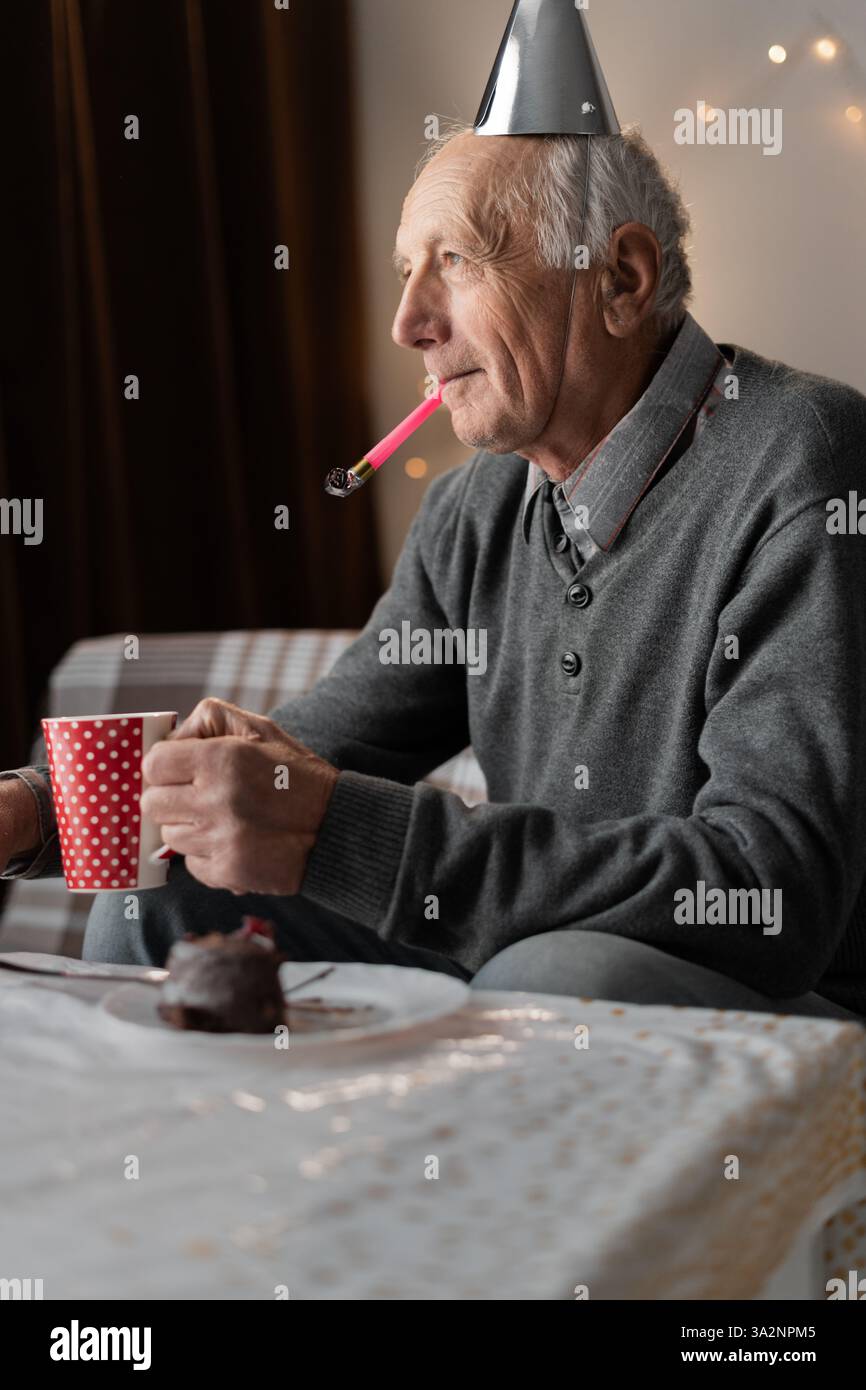 Unhappy retired man wearing cone hat with horn in mouth looking away ...