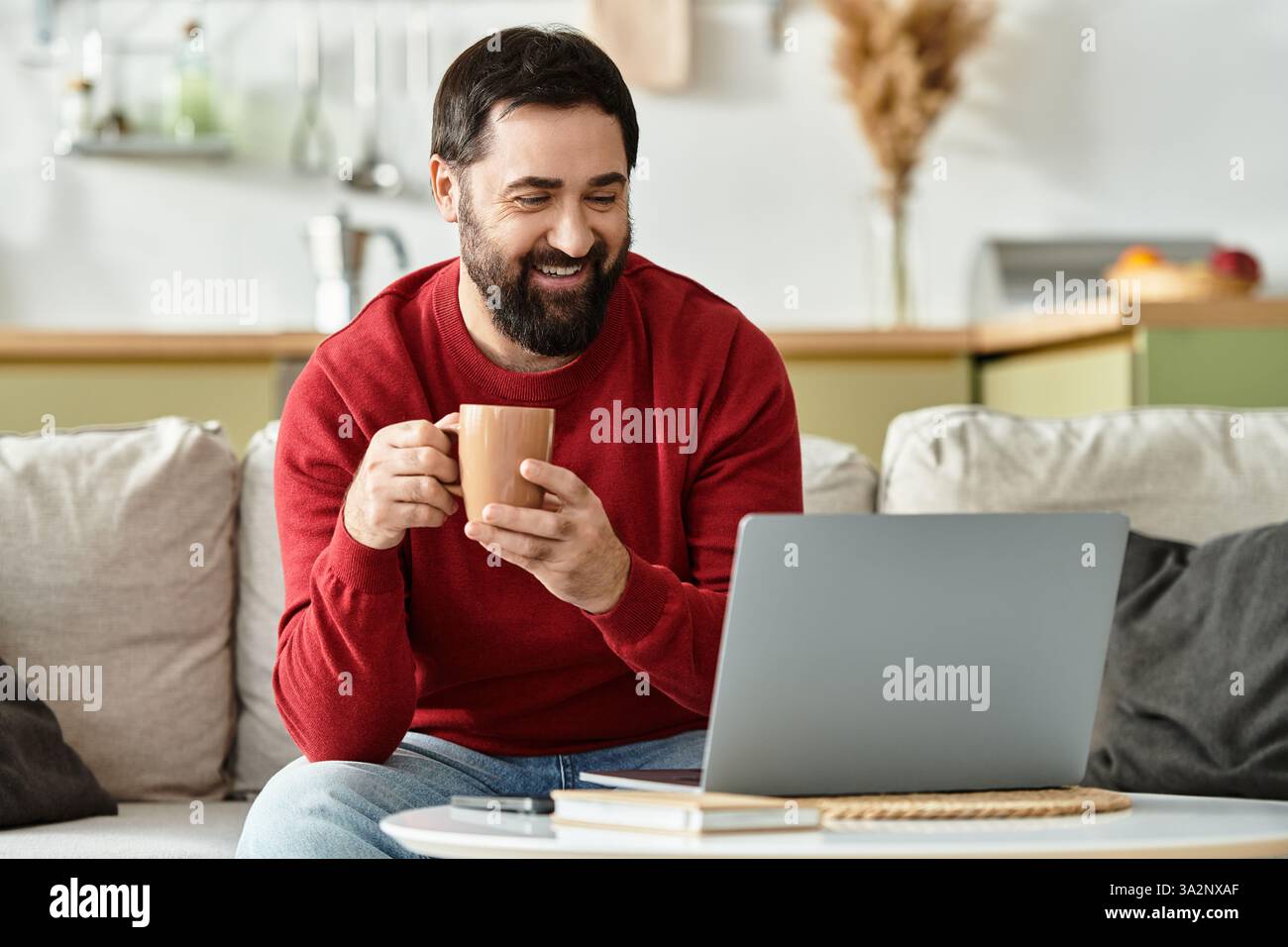 A gentle man relaxes on a couch, sipping coffee and engaging with his ...