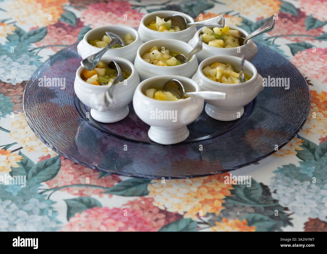 White cups with chopped fresh fruit and a spoon. Blue glass plate and ...