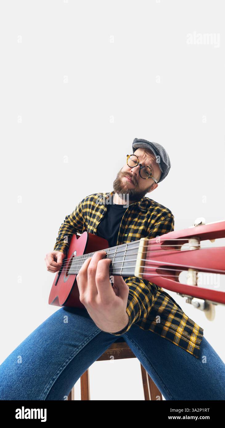 Focused musician in checkered shirt playing red acoustic guitar, deeply ...