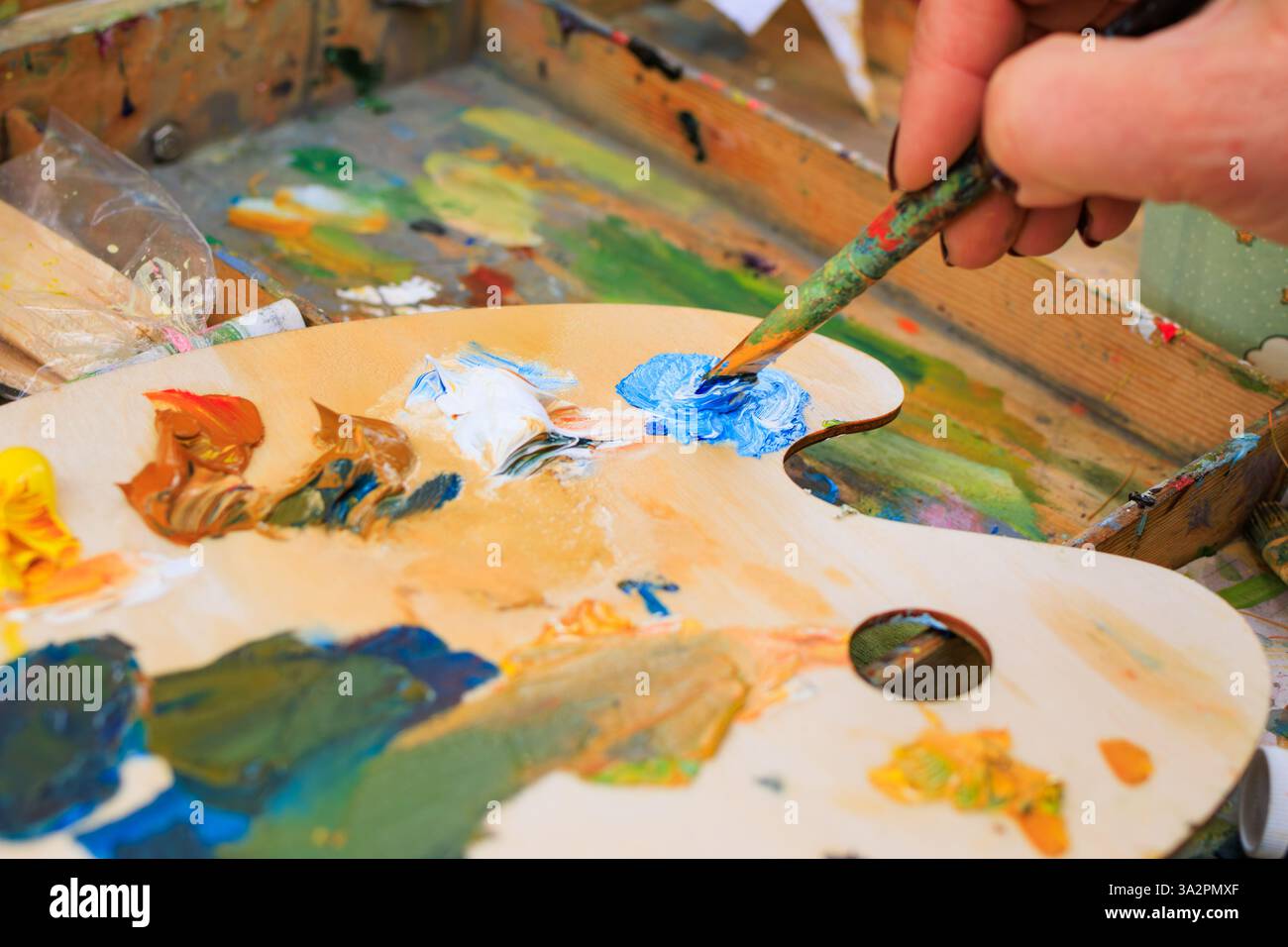 An artists hand mixing blue paint on a wooden palette with a brush ...