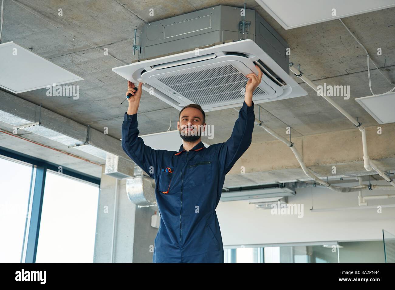 A man repairs the ventilation system, the device hangs on the ceiling ...