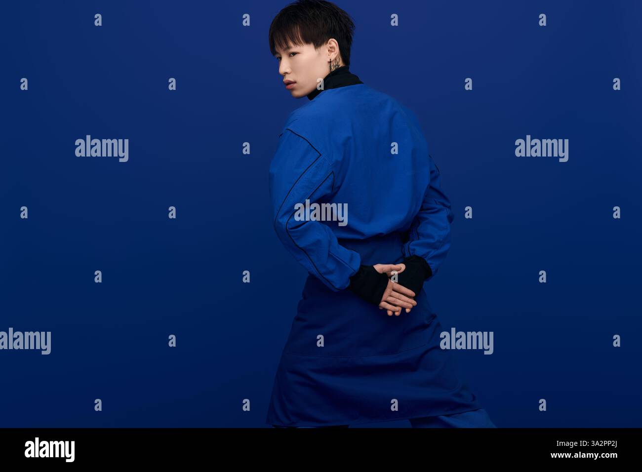 A young, attractive Asian man stands with his back turned, hands ...