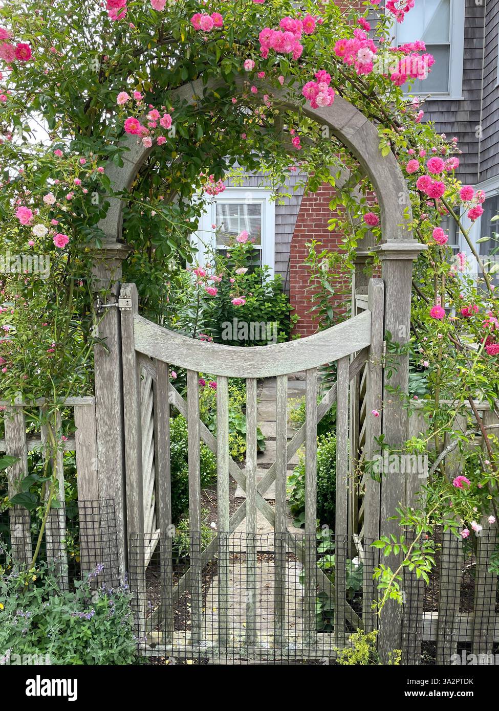 A cedar wood arbor with flowers blooming serves as the entrance to the ...