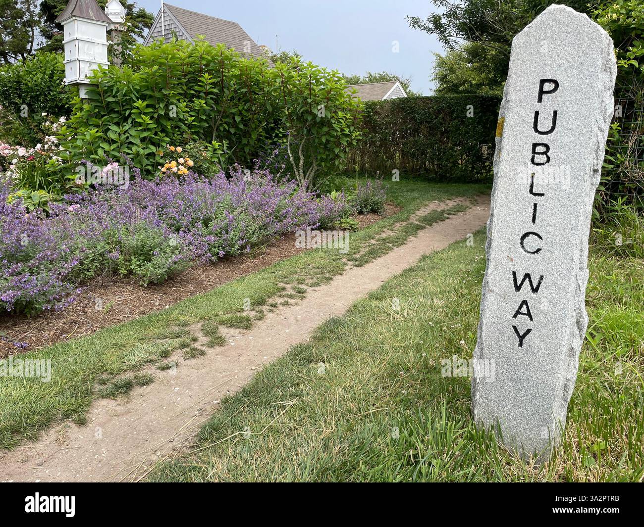A stone pillar marks the path of a public walkway, passing a garden in ...