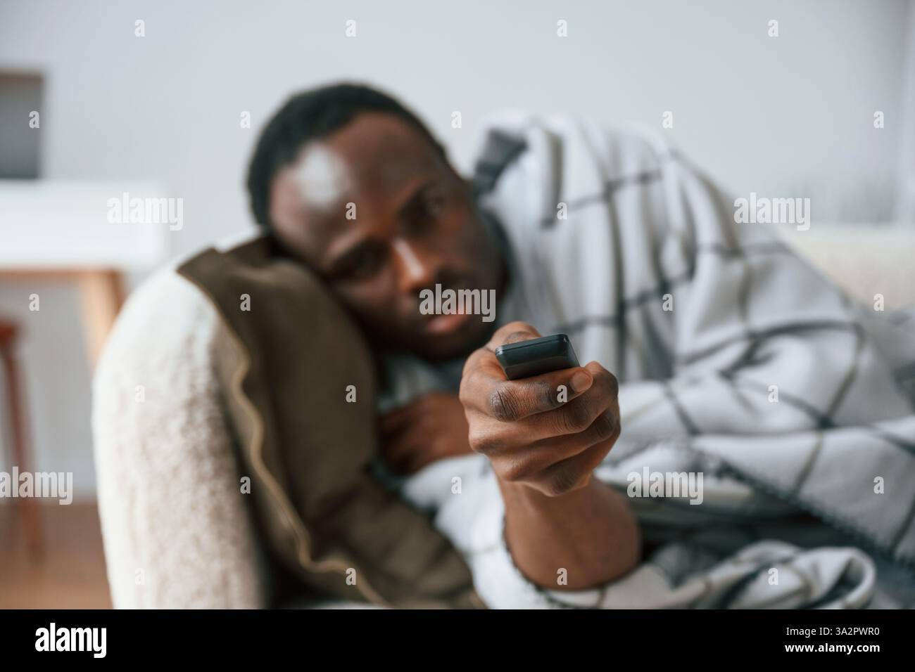 Holding TV remote controller. Lying down. Sick black man is at home ...
