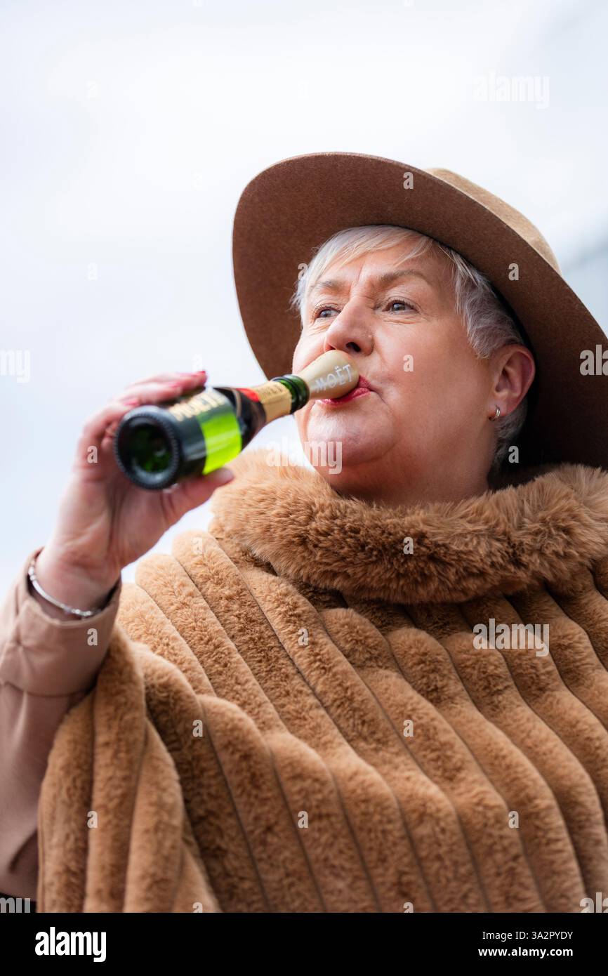 Cheltenham, England. March 13, 2025. A lady drinks from a mini Moet ...