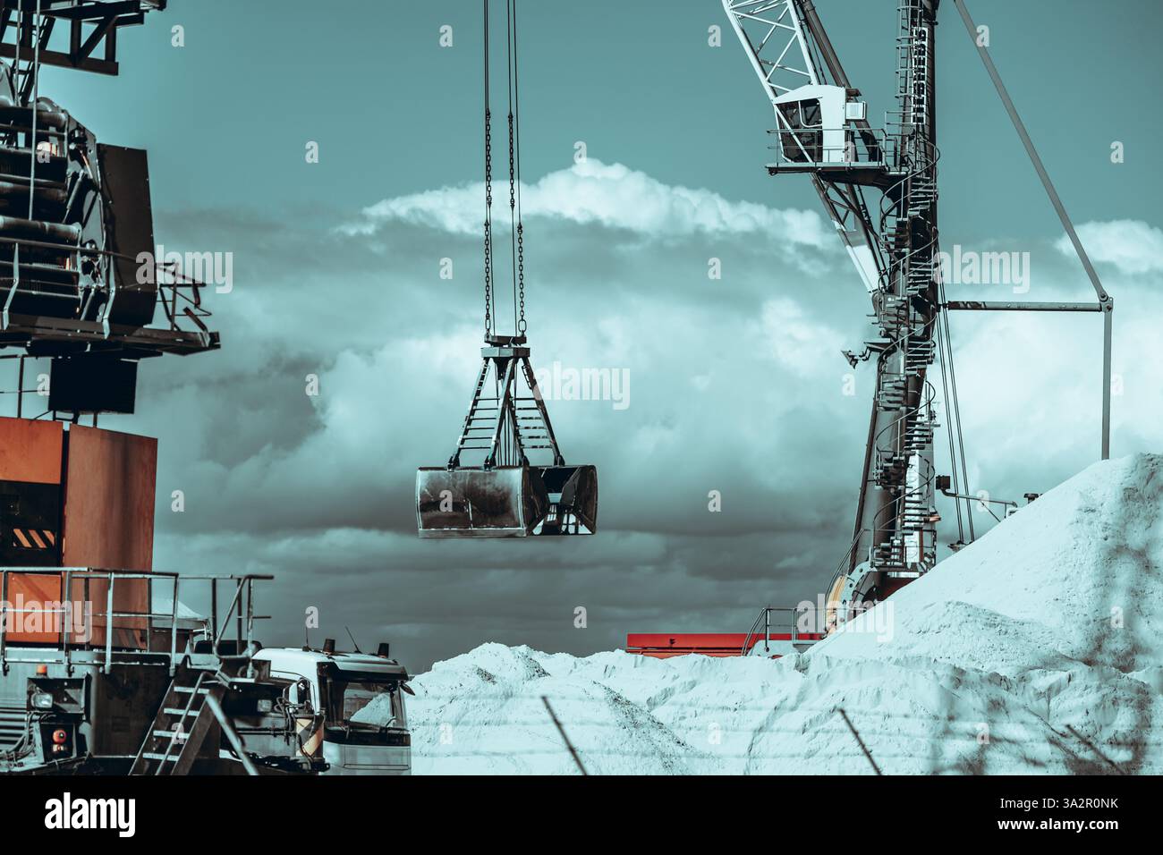 Industrial site with crane bucket lifting bulk material, machinery ...
