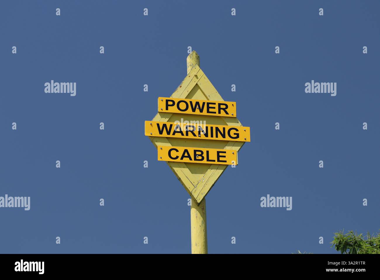 A wooden pale yellow diamond shaped warning sign with black text ...