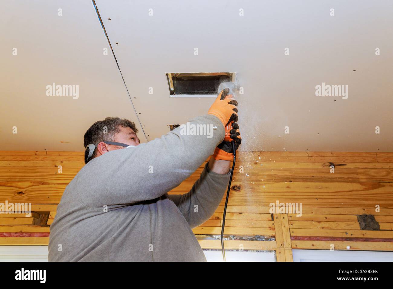 Contractor works on ceiling vent, using power saw tools in room during ...