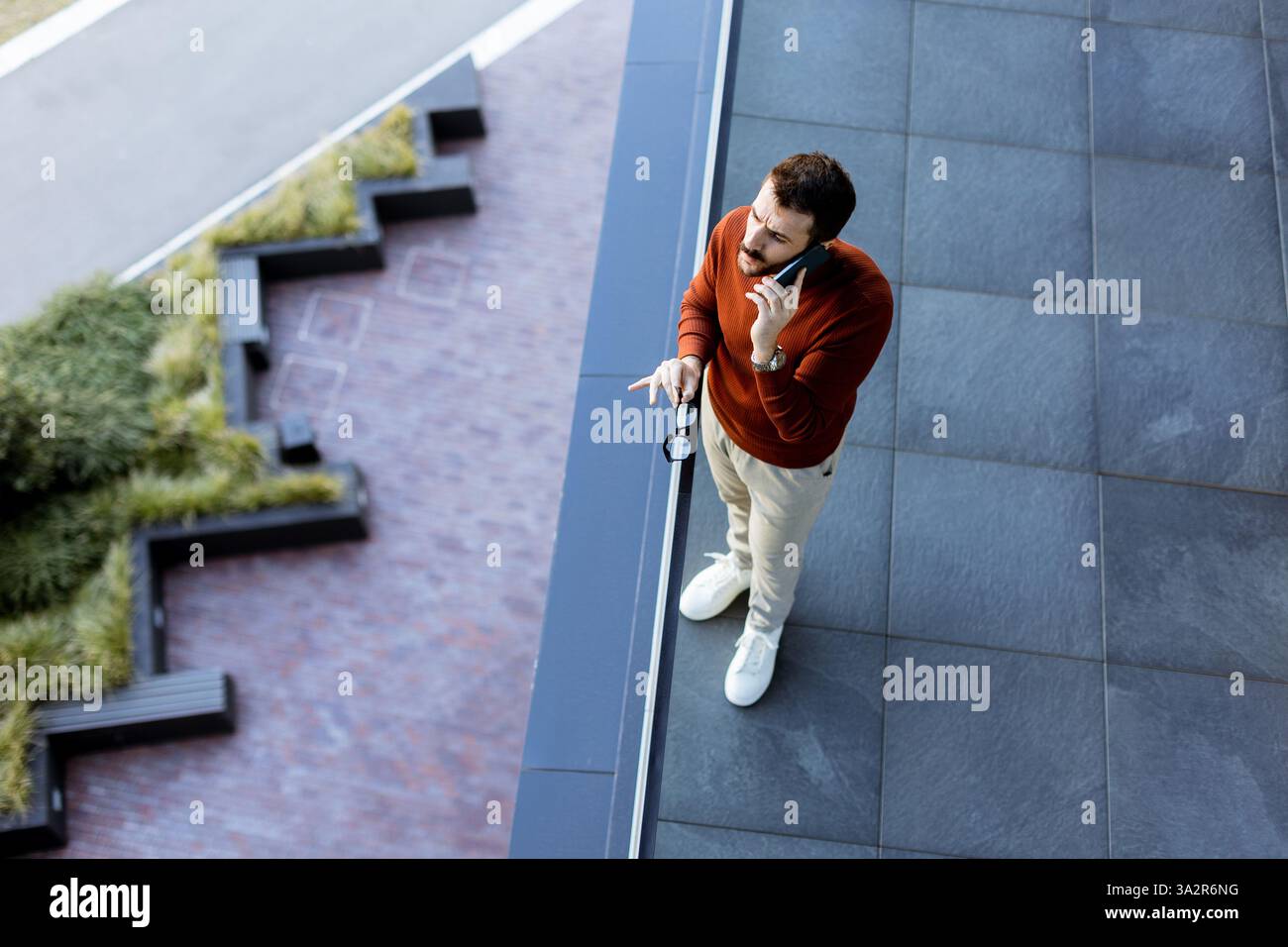 A young man stands on a sleek balcony while engaged in an animated ...