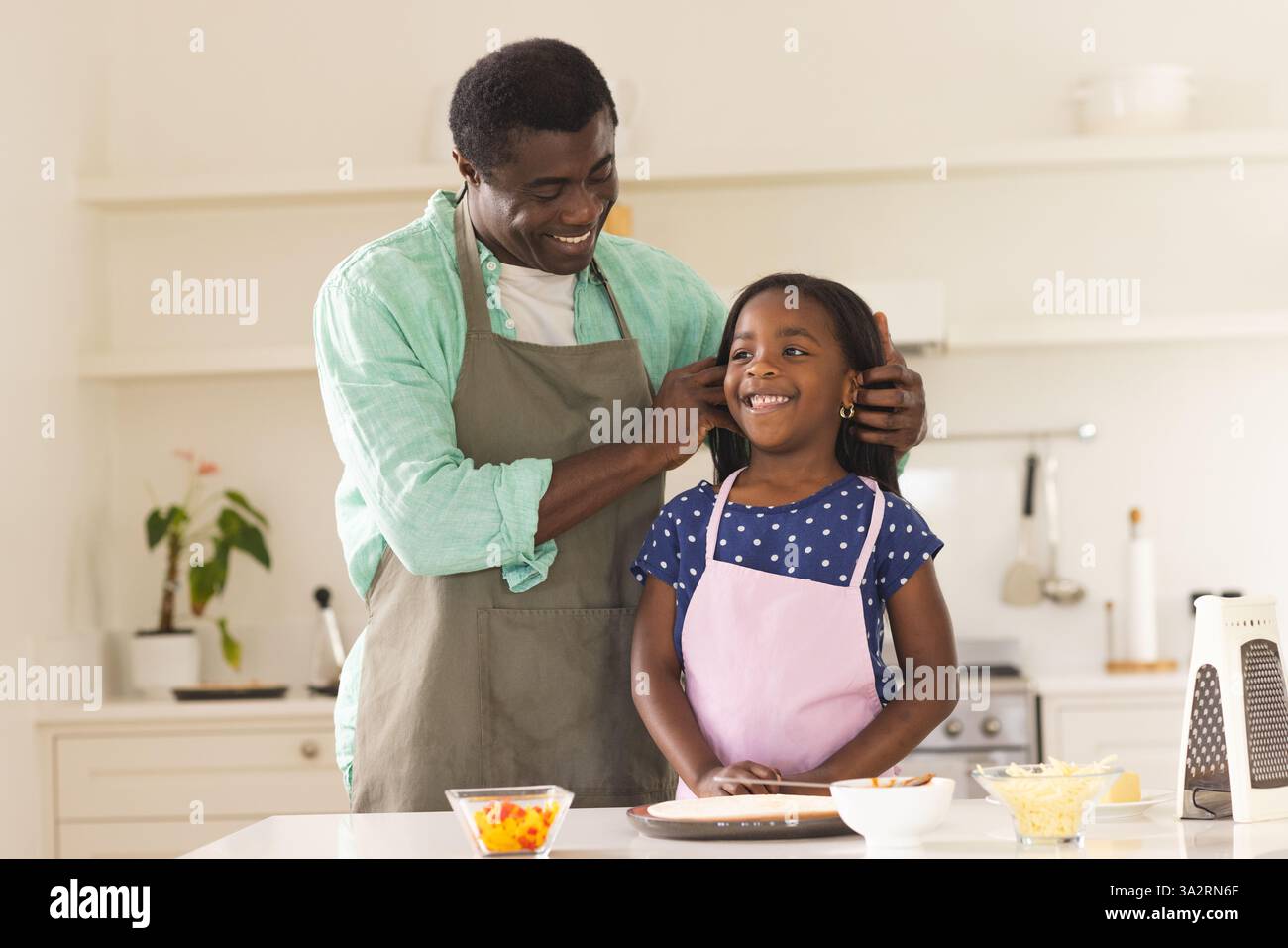 In kitchen, African American father helping daughter with apron ...