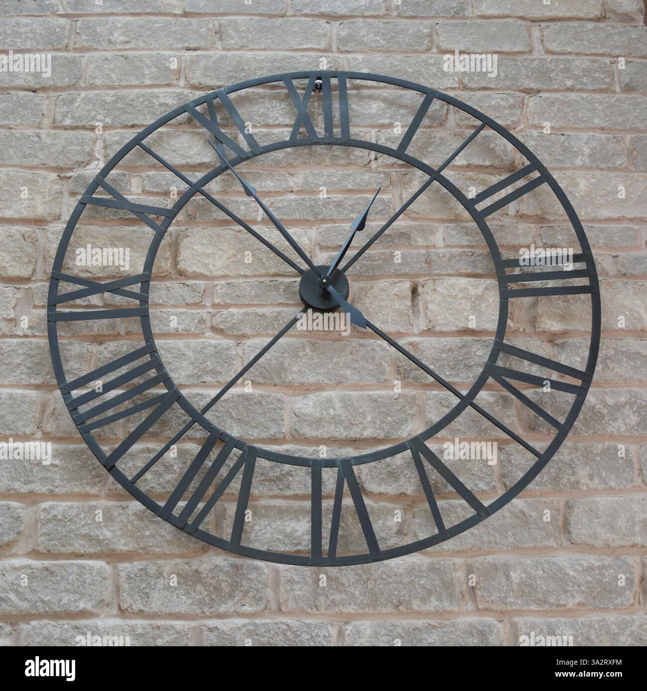 A large metal wire frame clock with roman numerals hangs on a grey ...