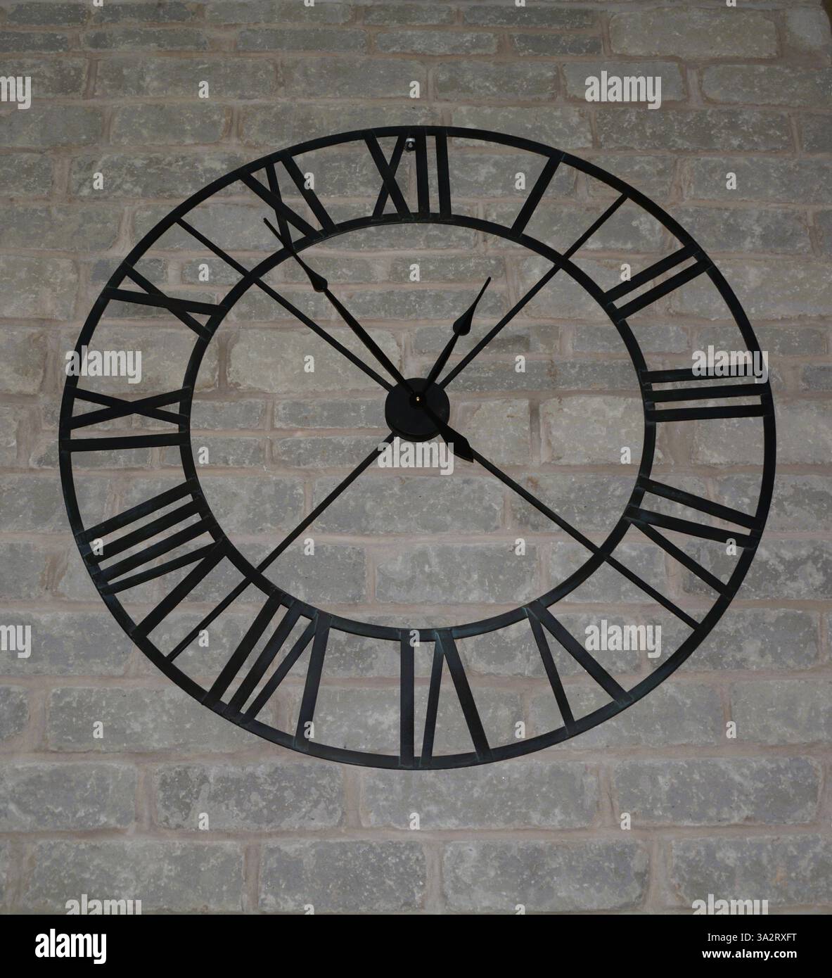 A large metal wire frame clock with roman numerals hangs on a grey ...