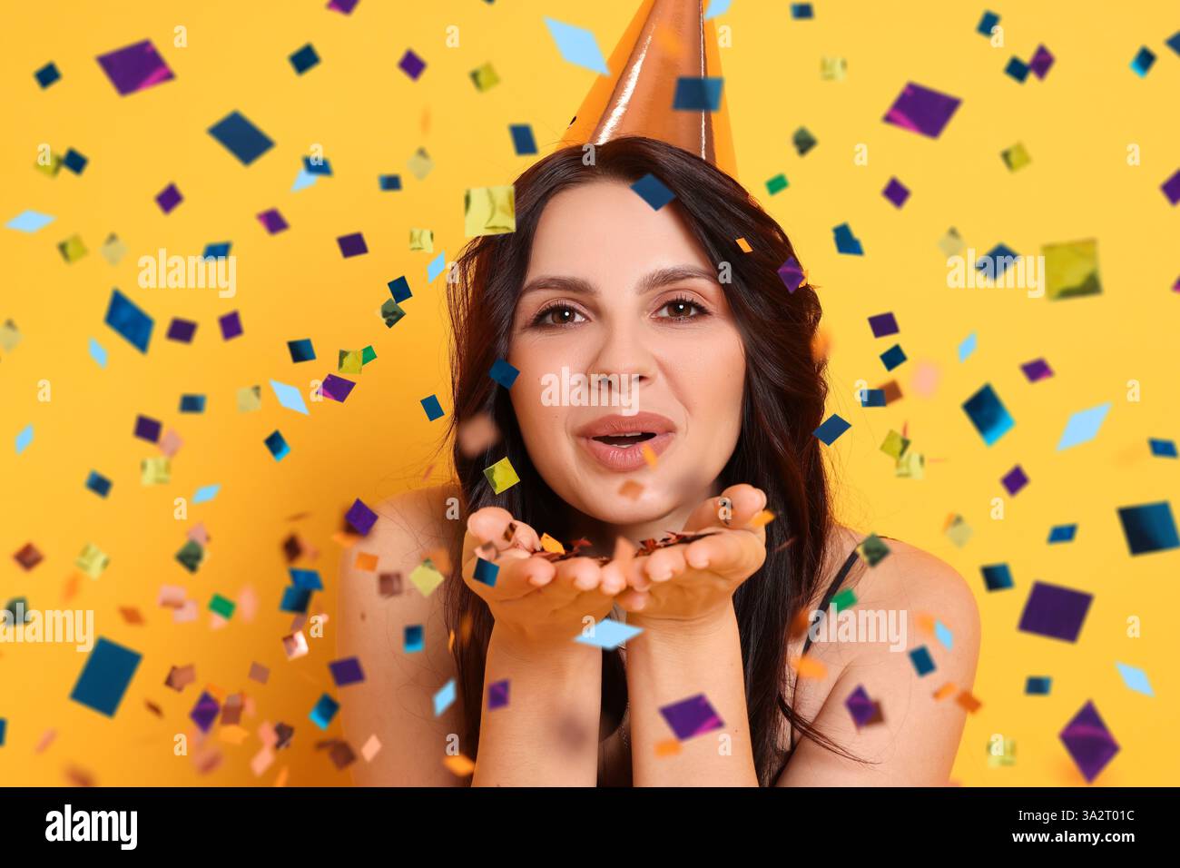 Beautiful woman in conical paper hat blowing confetti off hands on ...