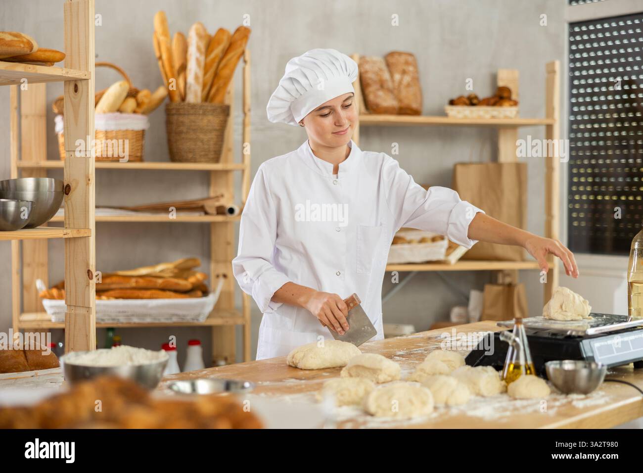 Teenage girl cutting and weighing dough on scales in bakehouse Stock ...