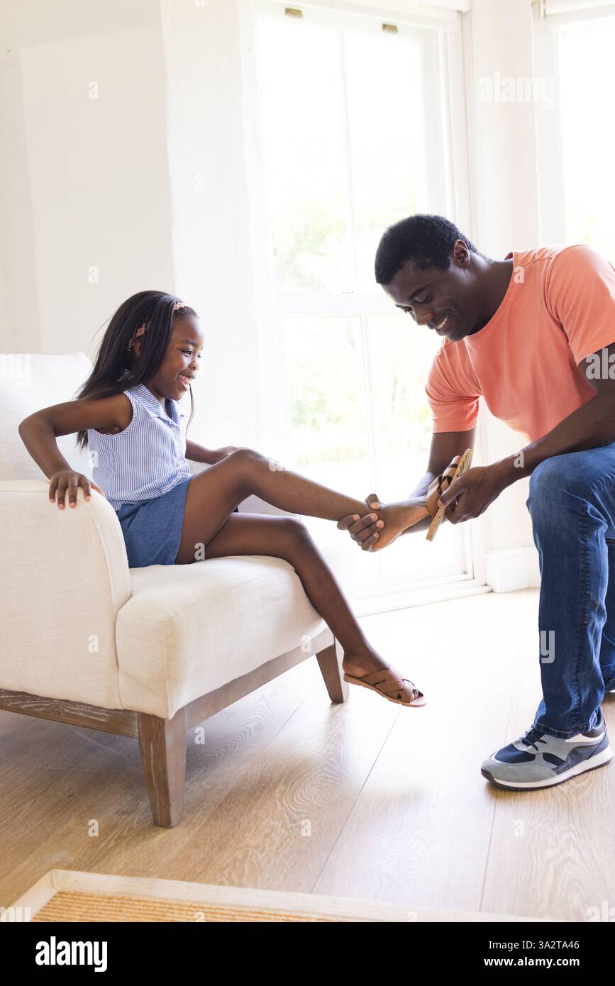 African American father helping daughter put on shoes at home, both ...