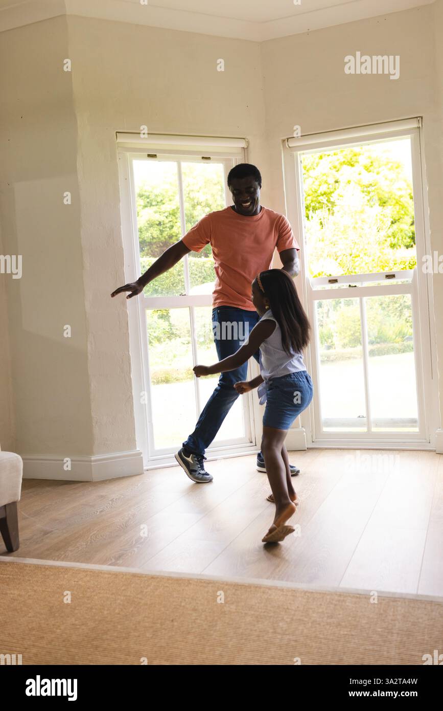 African American father and daughter dancing joyfully at home, enjoying ...