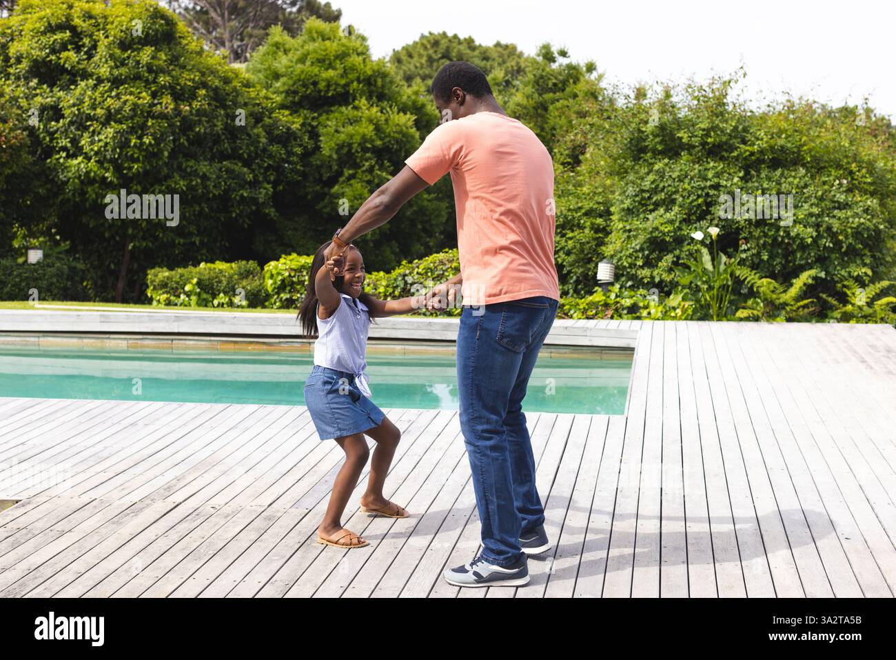 African American father and daughter dancing joyfully by poolside ...
