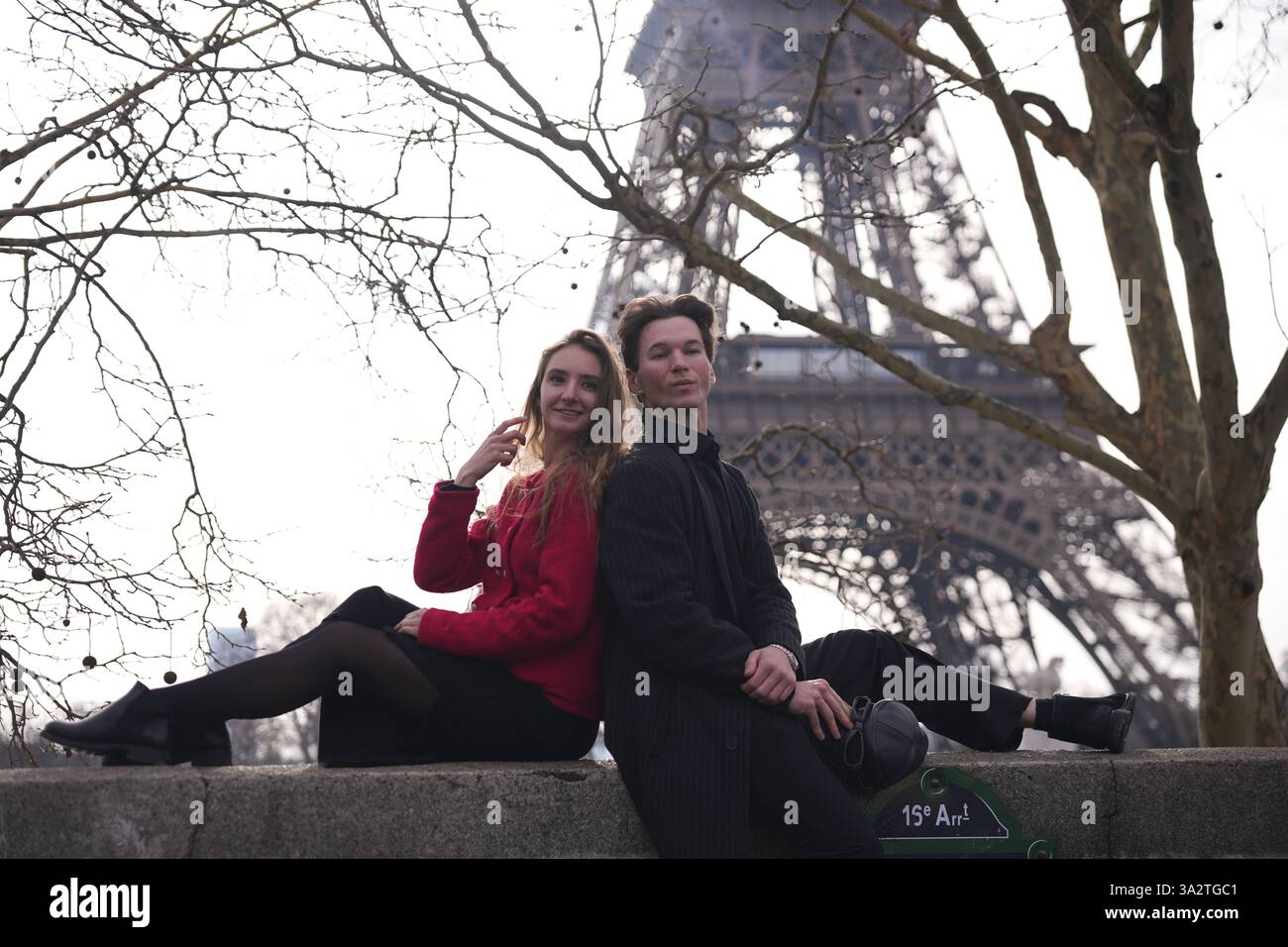A fashionable young couple leans back against each other on a stone ...