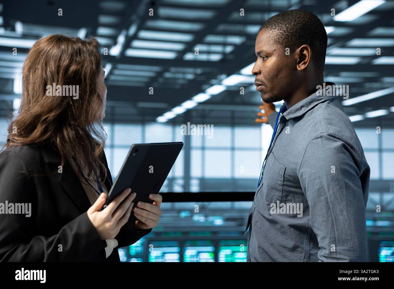 IT staff members in data center using tablet, verifying compliance requirements of rigs. Man and ...