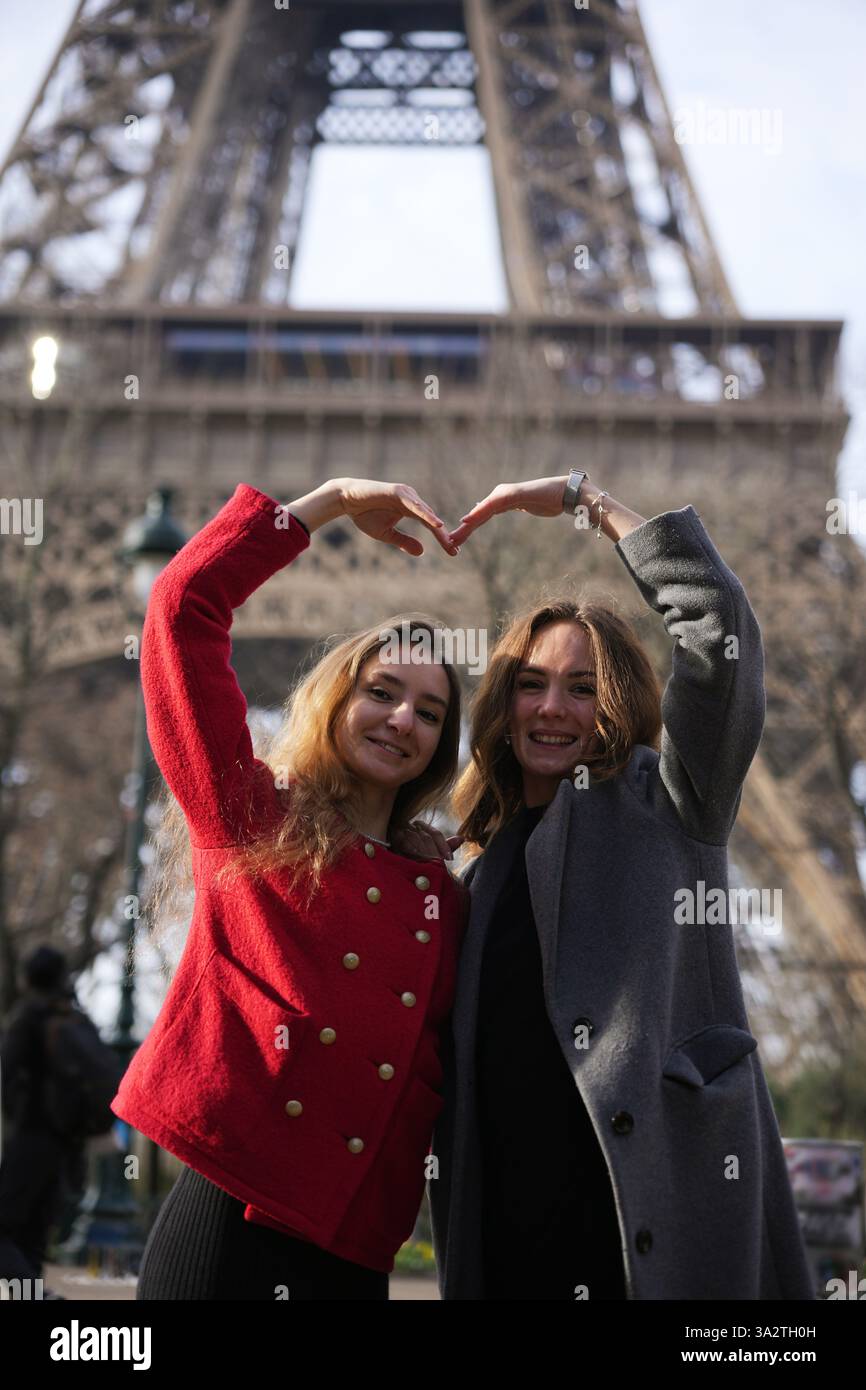 Two smiling friends pose in front of the Eiffel Tower, forming a heart ...