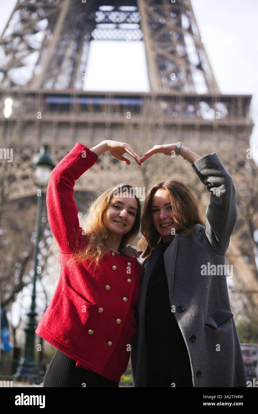 Two happy friends pose in front of the Eiffel Tower, forming a heart ...