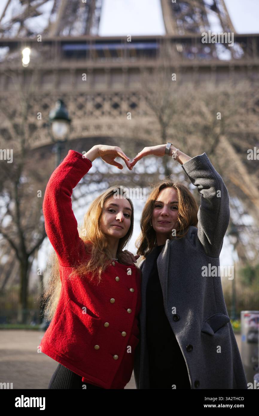 Two stylish friends pose in front of the Eiffel Tower, creating a heart ...