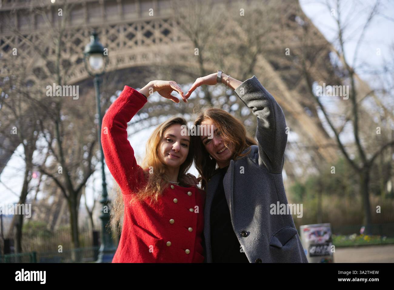 Two happy friends pose in front of the Eiffel Tower, forming a heart ...