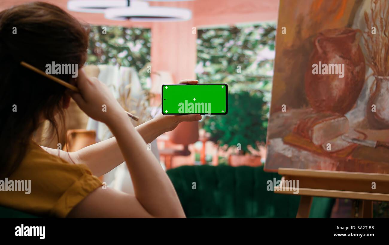 Female artist holding device with green screen in art and craft atelier, admiring rustic artwork ...