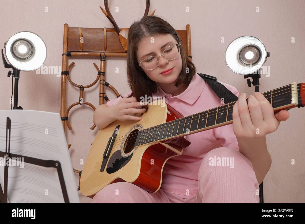 Young woman guitarist in eyeglasses practices strumming technique on ...