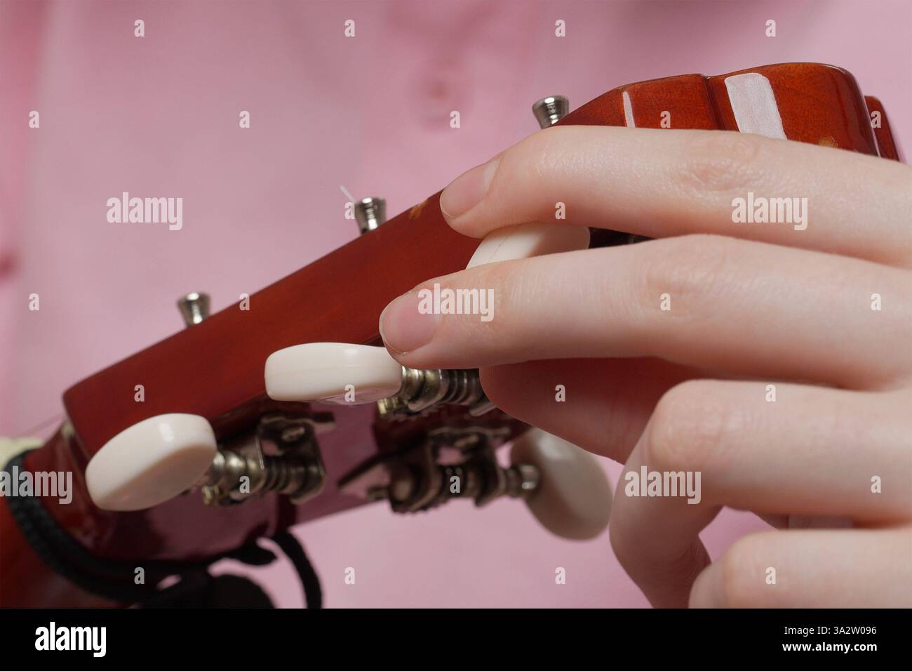 Extreme close-up female fingers tuning guitar, tightening and loosening strings before beginning ...